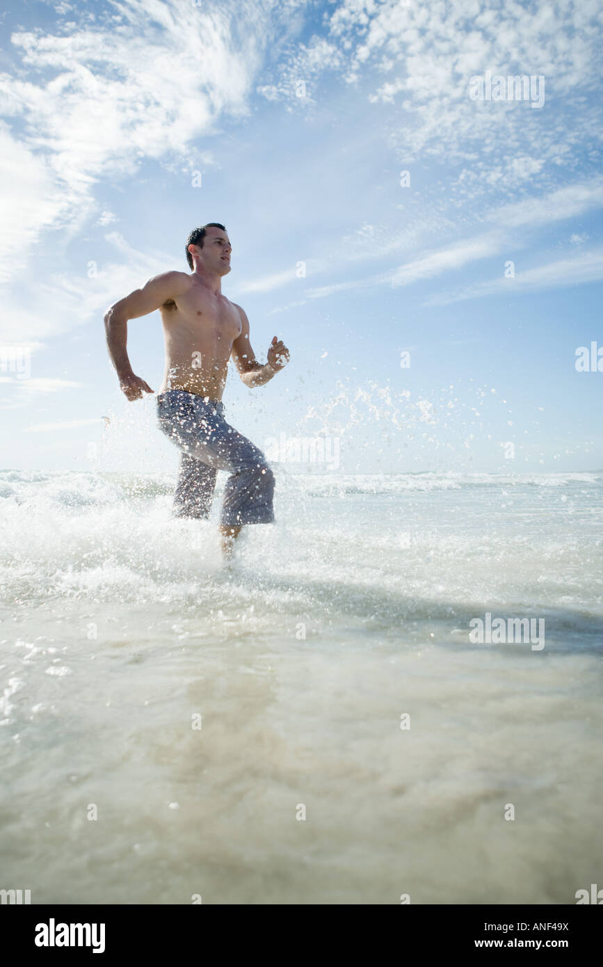 Young man running through surf, low angle view Stock Photo - Alamy