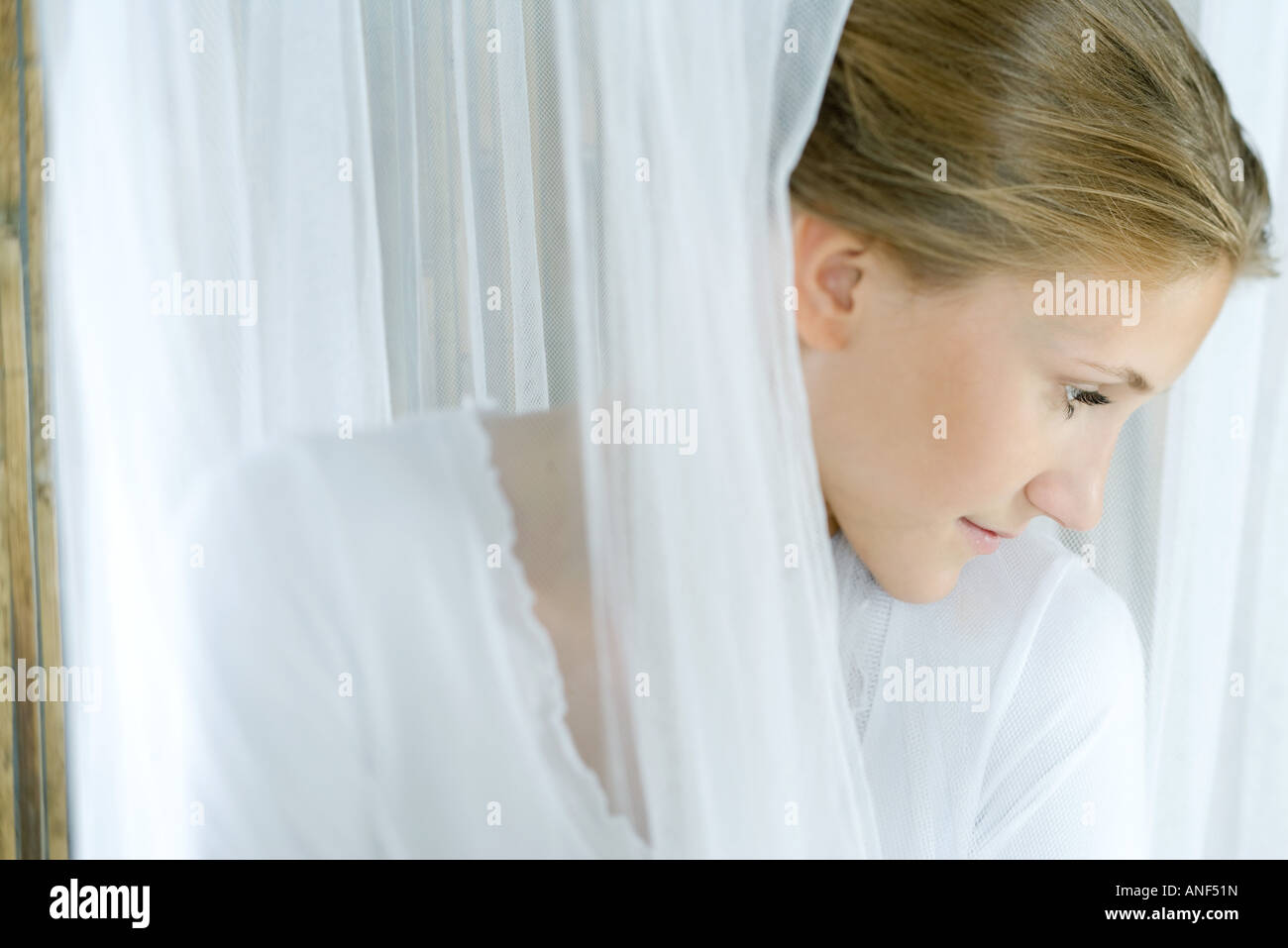 Young woman looking through translucent curtains, head and shoulders ...