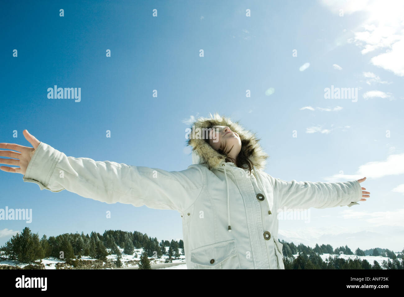 Teen girl standing in snowy landscape with arms out, head back, low ...