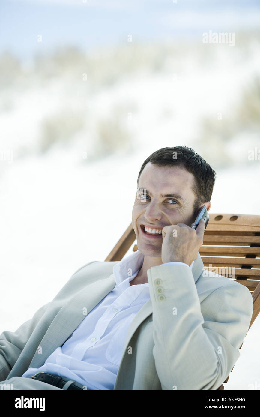 Businessman sitting in deck chair at beach, using cell phone Stock ...