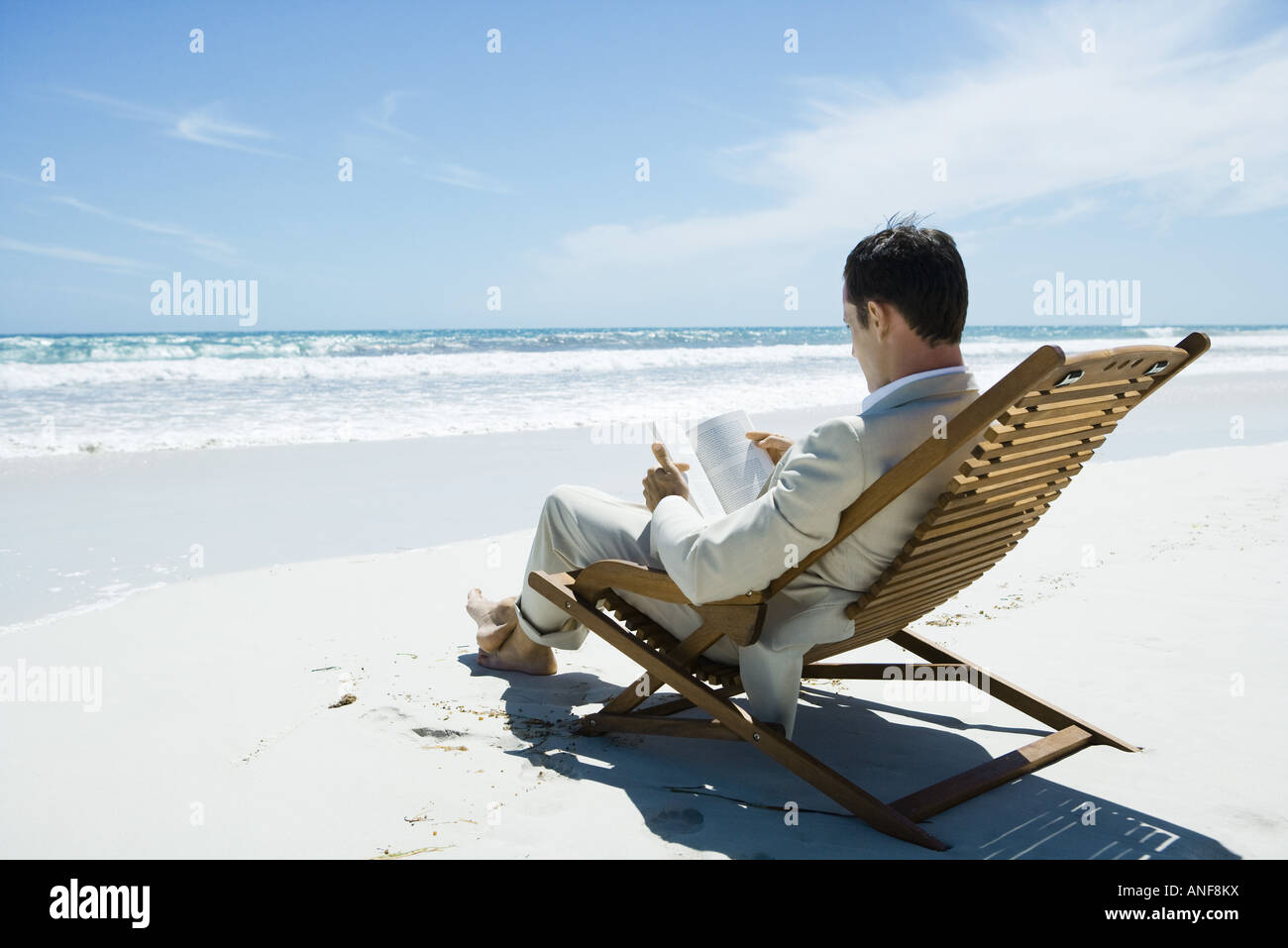 Businessman sitting in deckchair on beach, reading book Stock Photo - Alamy