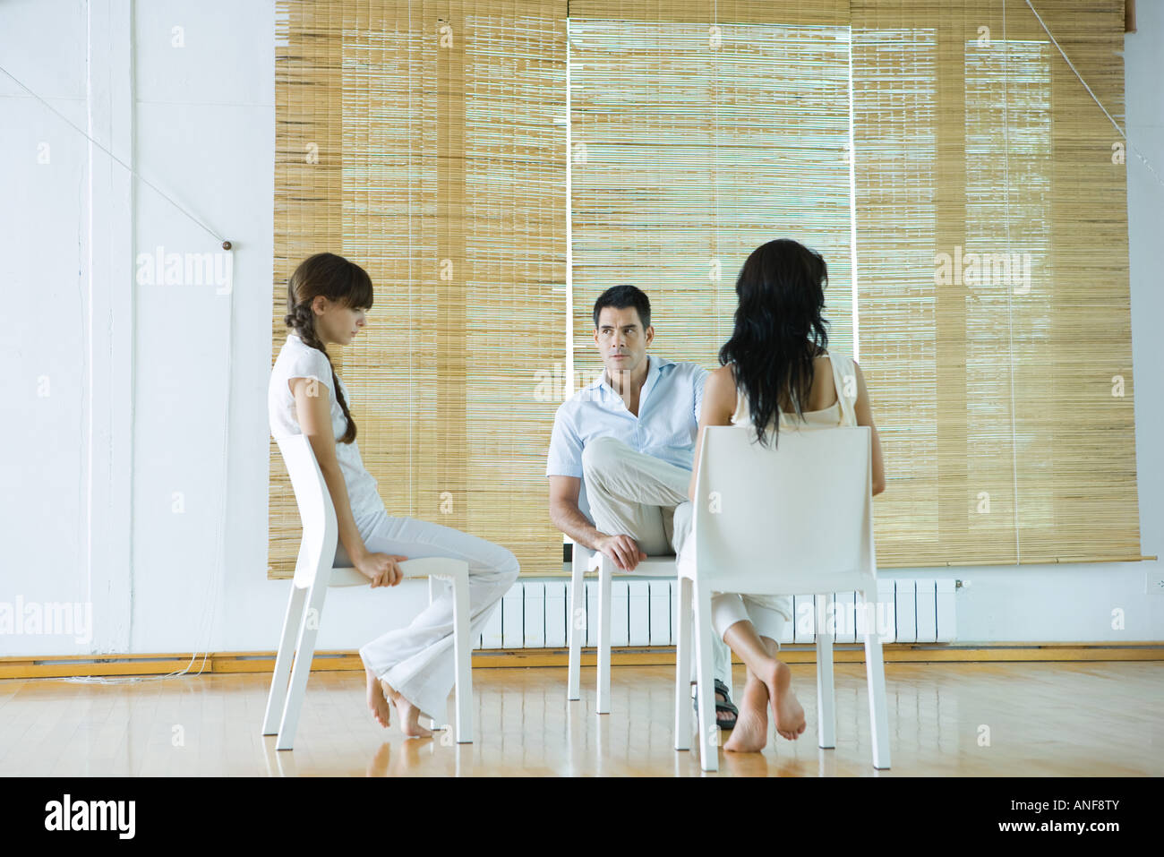 Three adults sitting in chairs, having therapy session, looking serious ...