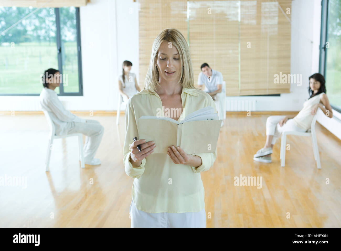 Woman leading group therapy session, reading from book, facing camera ...