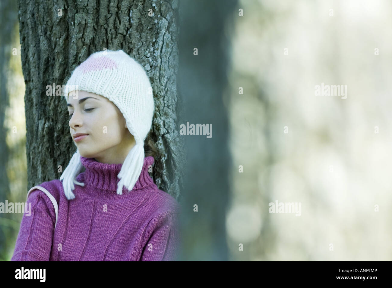 Young woman wearing knit hat, leaning against tree, eyes closed Stock ...