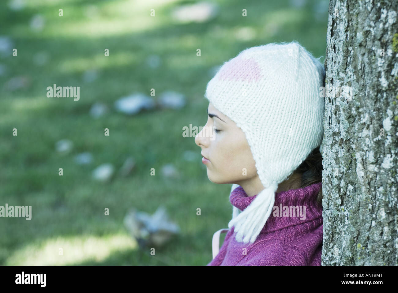 Young woman wearing knit hat, leaning against tree, eyes closed, side ...