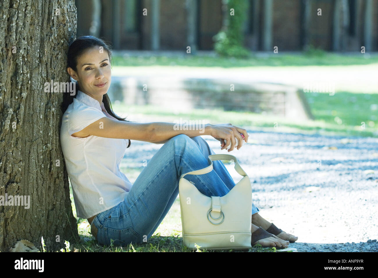 Woman sitting on ground, leaning against tree Stock Photo - Alamy