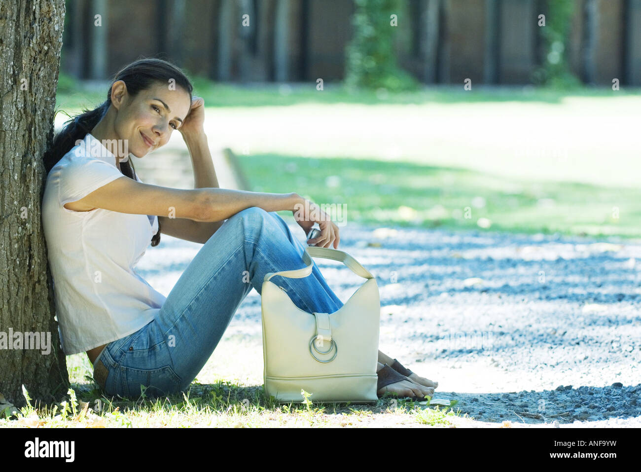 Woman sitting on ground, leaning against tree Stock Photo - Alamy