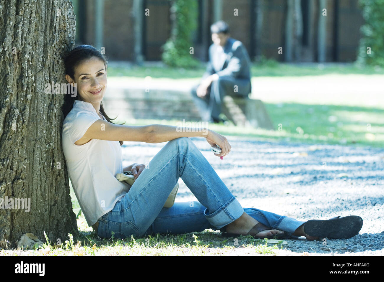 Woman sitting on ground, leaning against tree, smiling at camera Stock ...