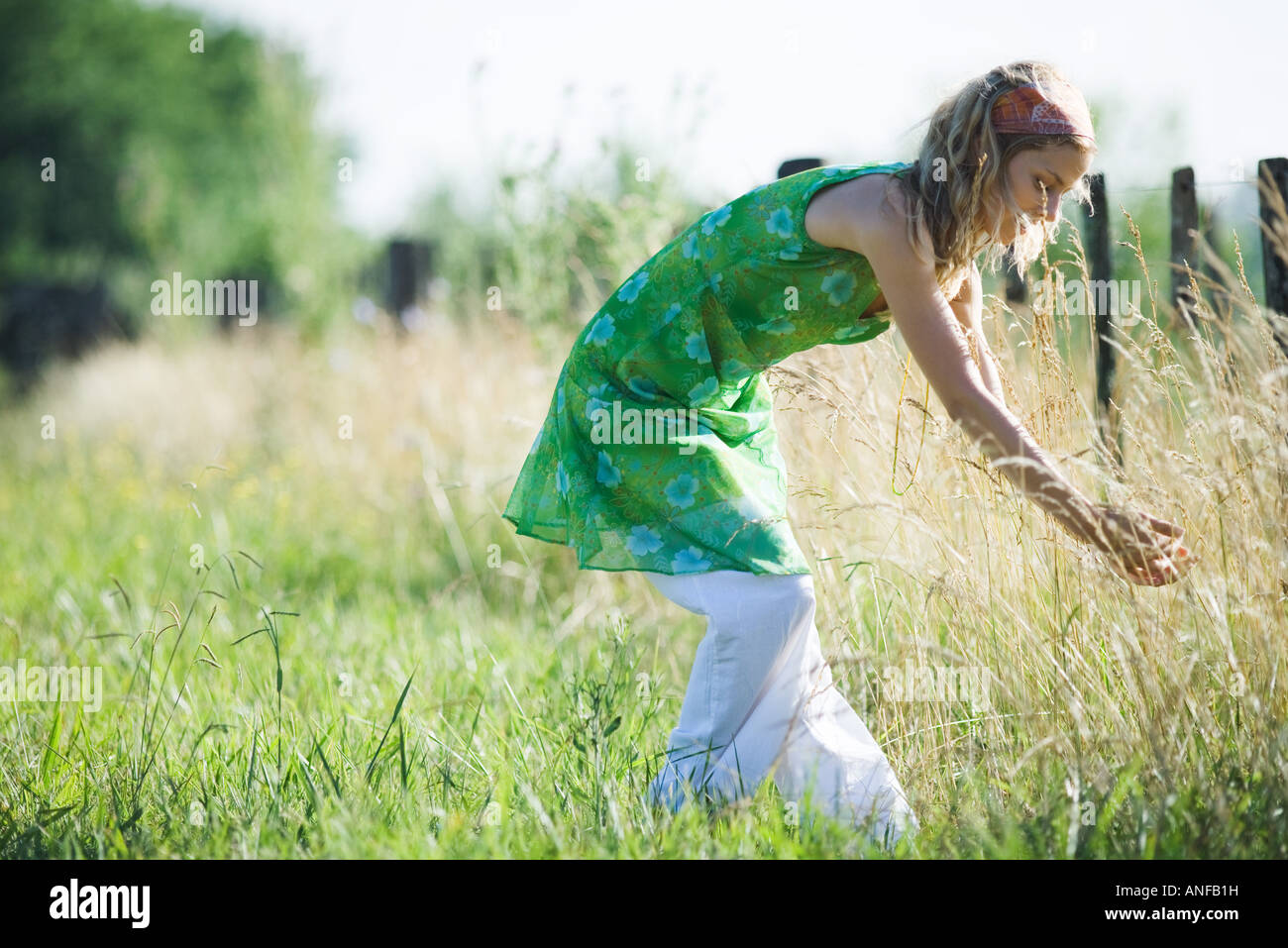 Young woman bending over to touch tall grass in rural field Stock Photo ...