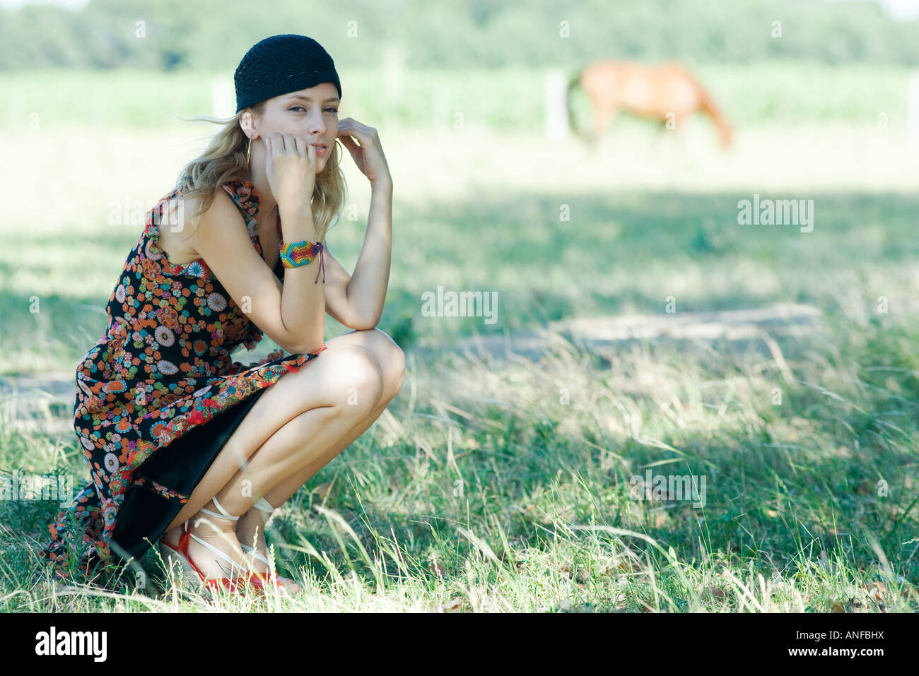 Young woman crouching in field, looking at camera Stock Photo - Alamy
