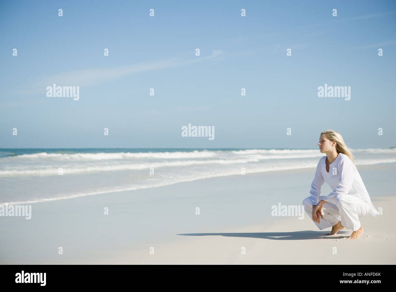Young woman crouching on beach Stock Photo - Alamy