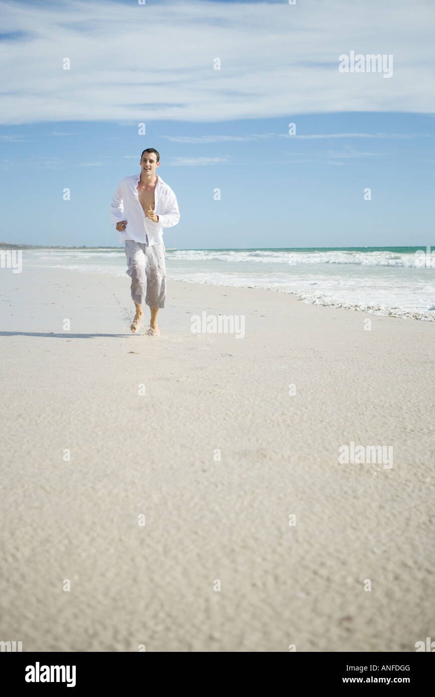 Young man running through surf on beach, front view Stock Photo - Alamy