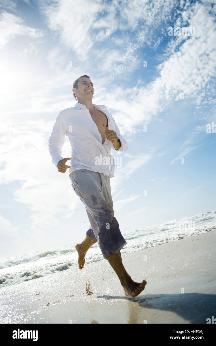 Young man running through surf on beach, low angle view, full length ...