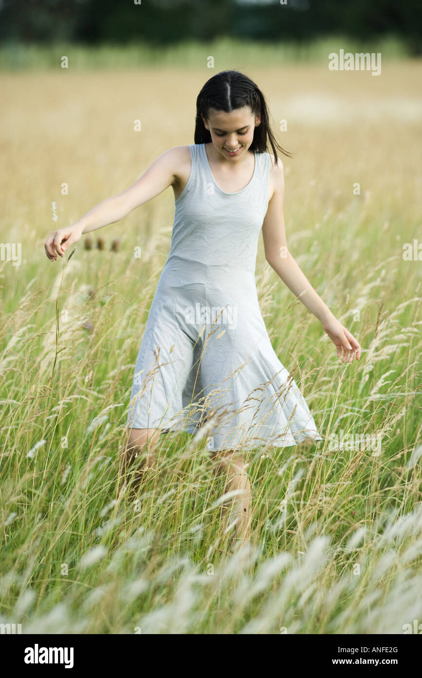 Teenage girl walking in field of tall grass with arms out, looking down ...