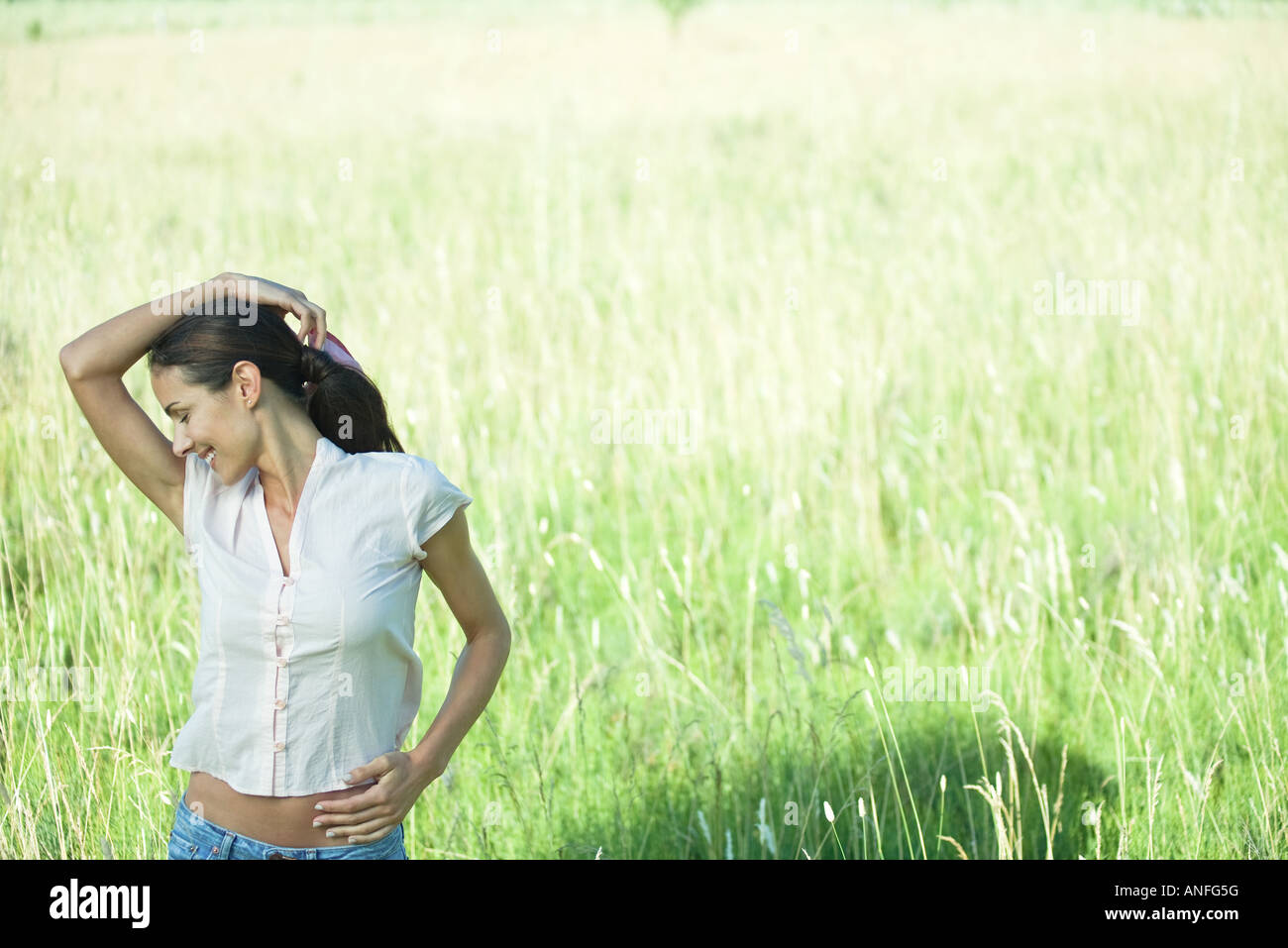 Woman standing in field, one hand on head, the other on hip, smiling ...