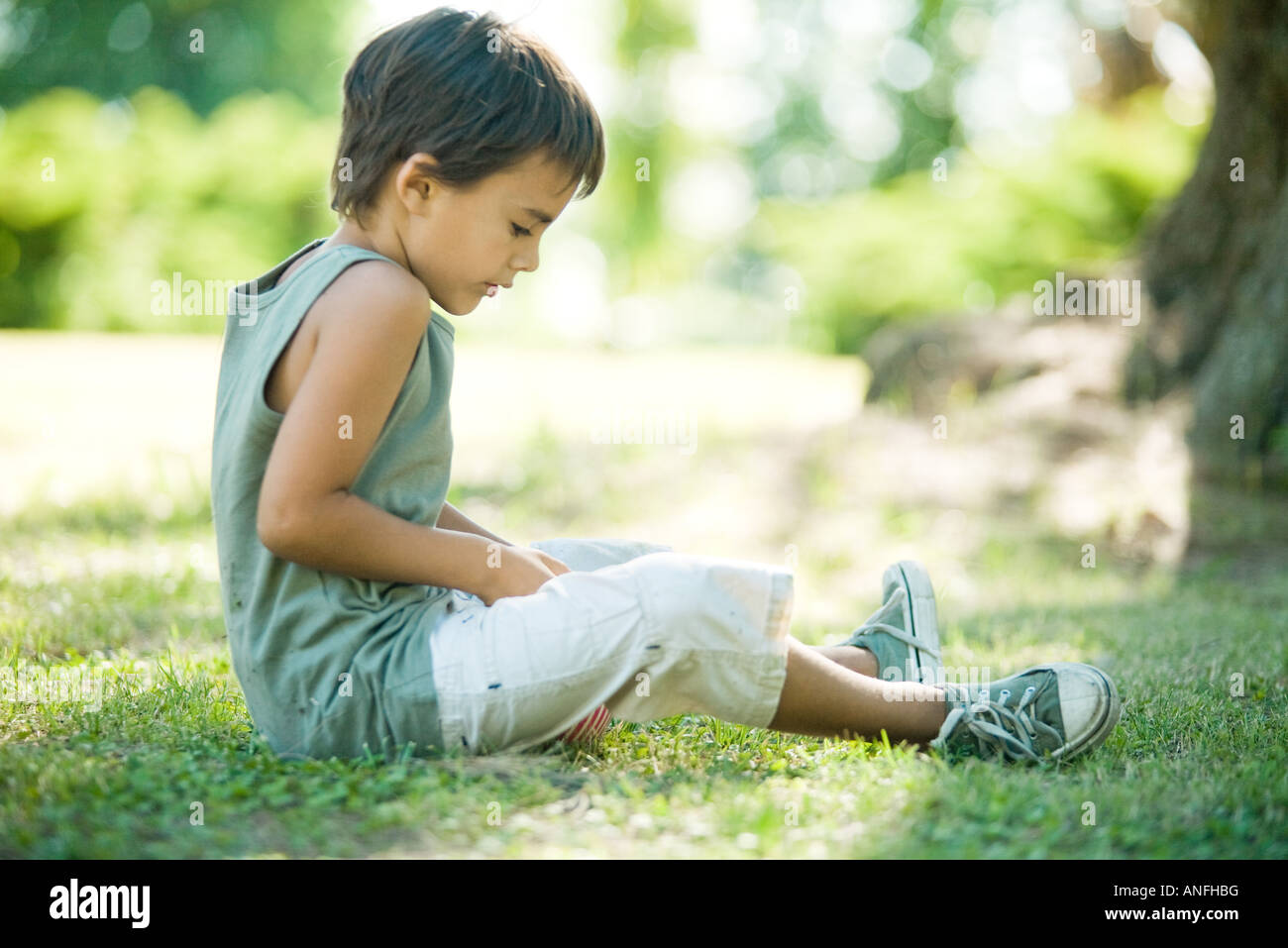 Little boy outdoors, sitting on grass, side view Stock Photo - Alamy