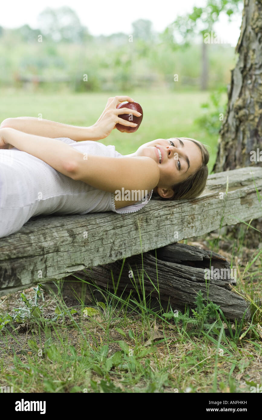 Woman lying on piece of wood, holding apple, looking at camera Stock ...