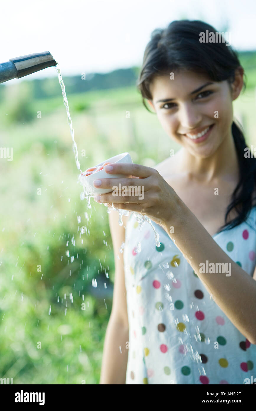Young woman rinsing off bowl of cherry tomatoes, smiling at camera ...