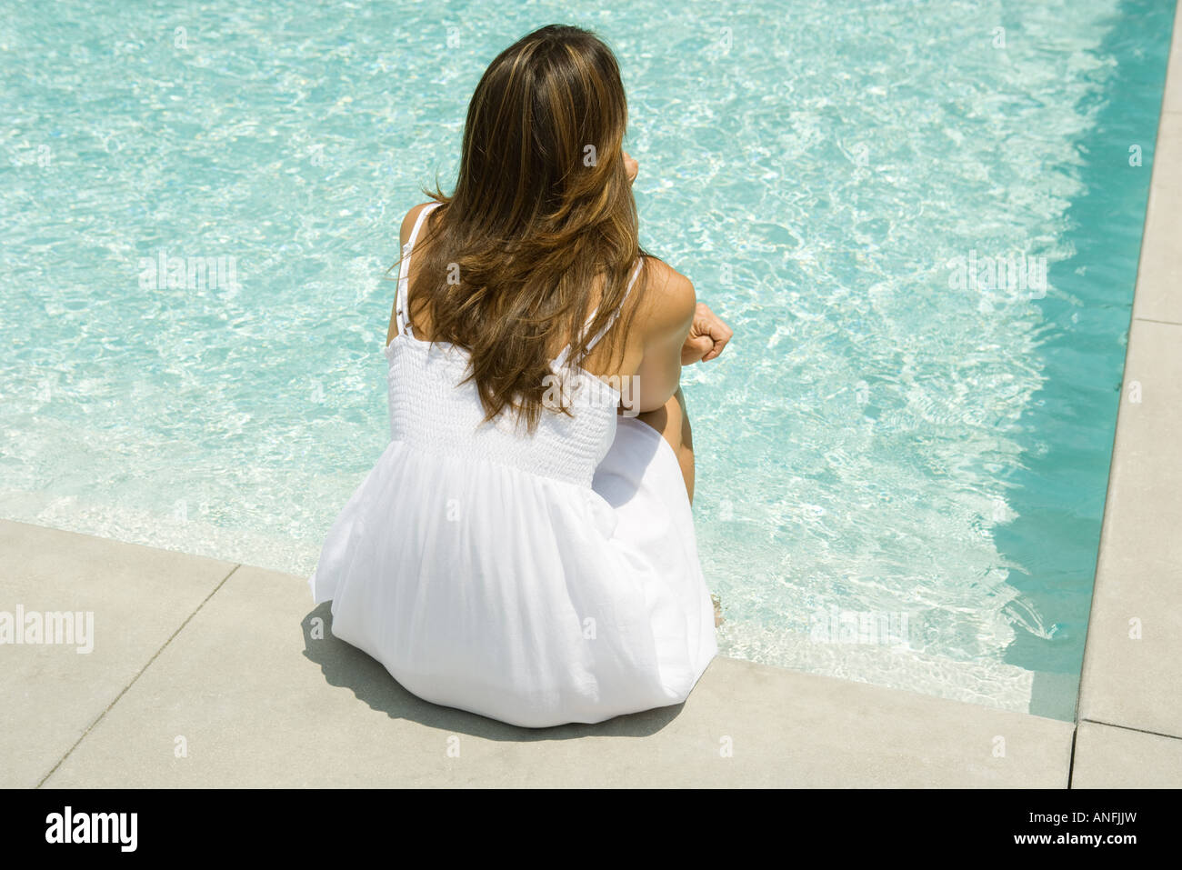 Woman sitting on edge of pool, rear view Stock Photo - Alamy