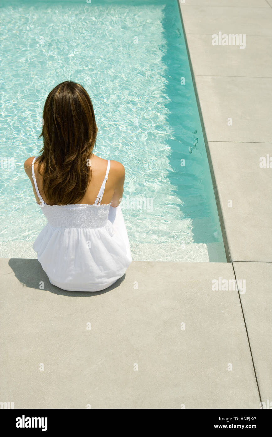 Woman sitting on edge of pool, rear view Stock Photo - Alamy