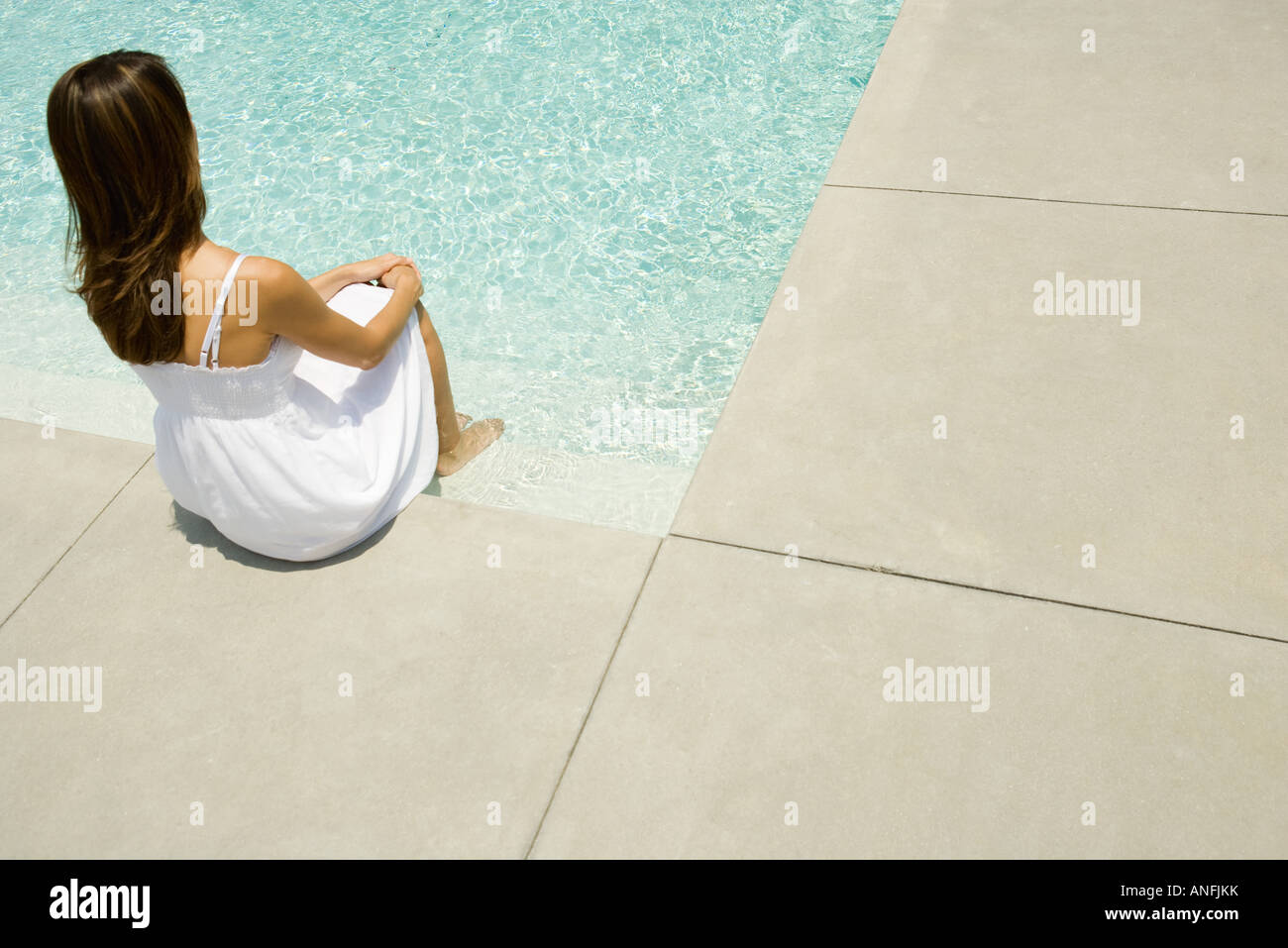 Woman sitting on edge of pool, rear view Stock Photo - Alamy
