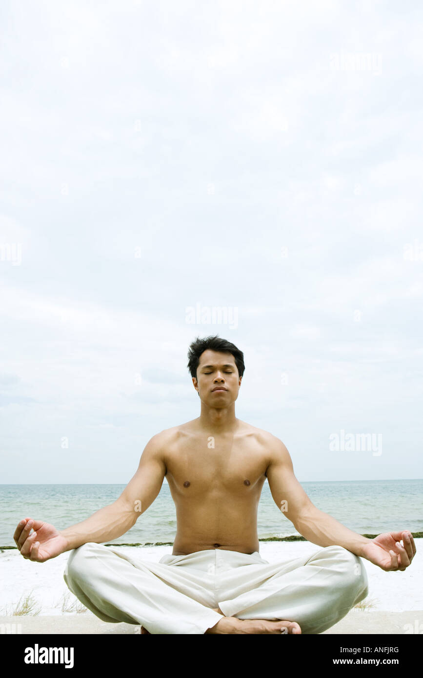 Barechested man sitting in lotus position, ocean in background Stock ...