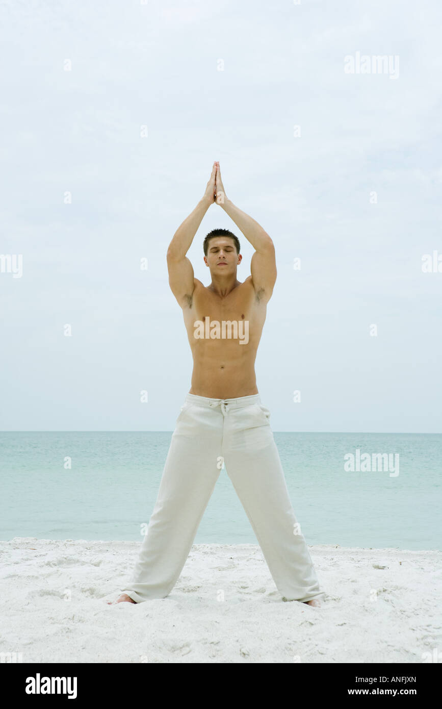 Man standing on beach, doing yoga, full length Stock Photo - Alamy