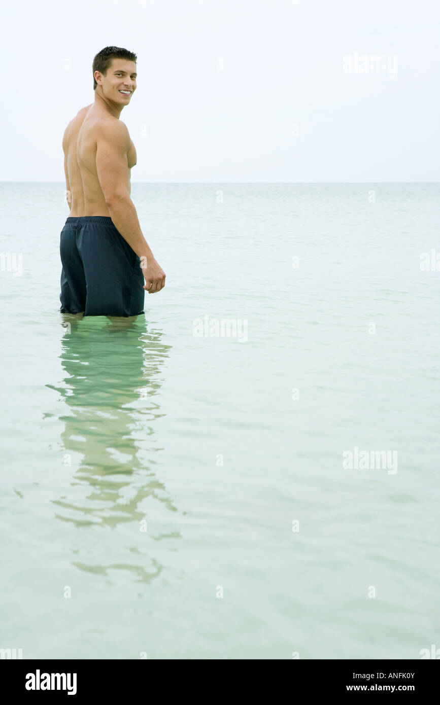 Man standing knee deep in ocean, smiling over shoulder at camera Stock ...