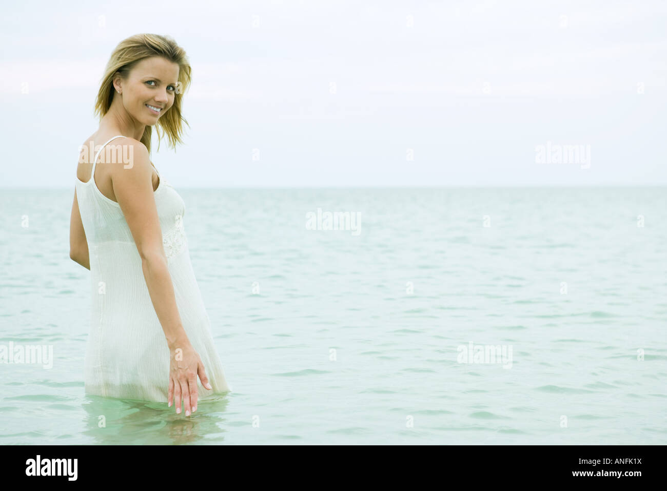 Woman standing thigh deep in ocean, looking over shoulder at camrea ...