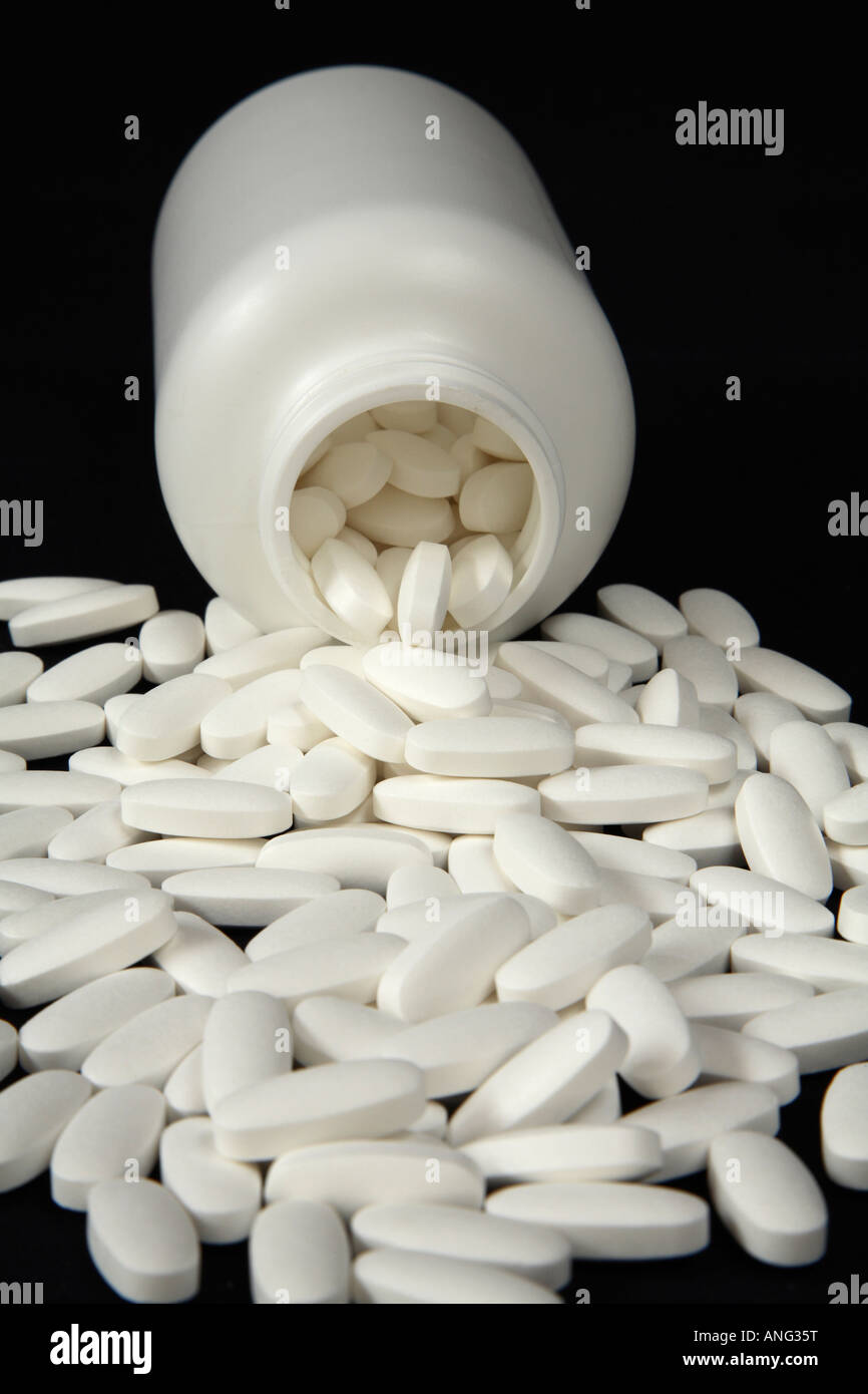 Plain white bottle spilling large pool of oval white caplets before it ...