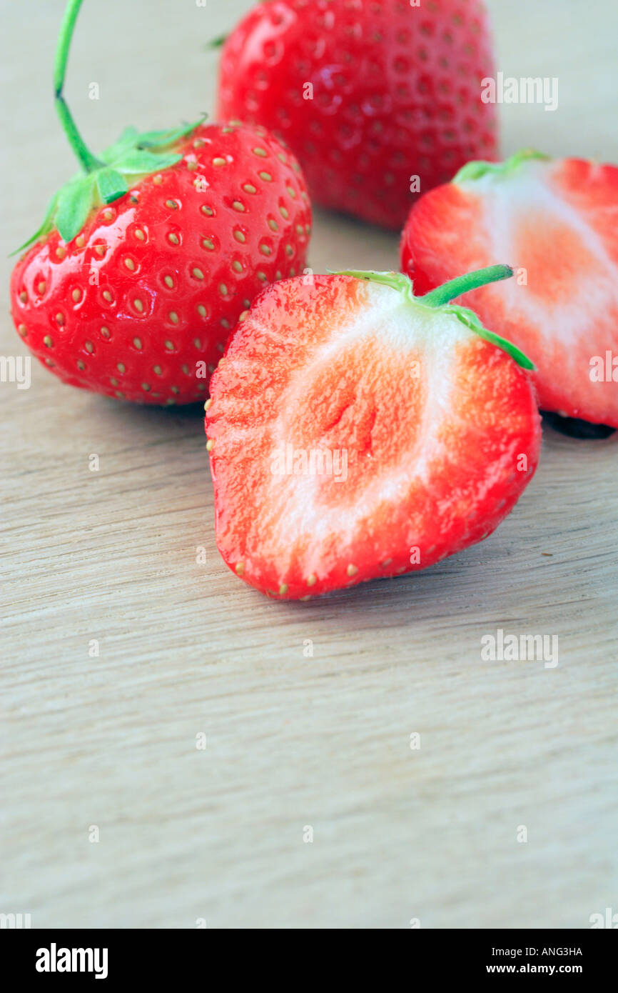 Three strawberries, one cut in half on chopping board Stock Photo - Alamy