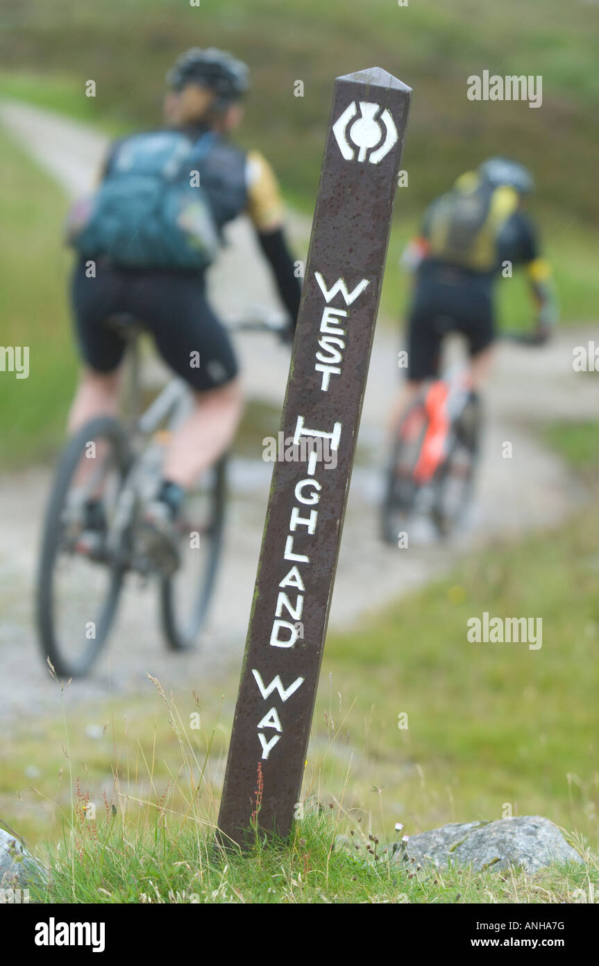 Mountain bikers ride by a West Highland Way long distance footpath sign ...