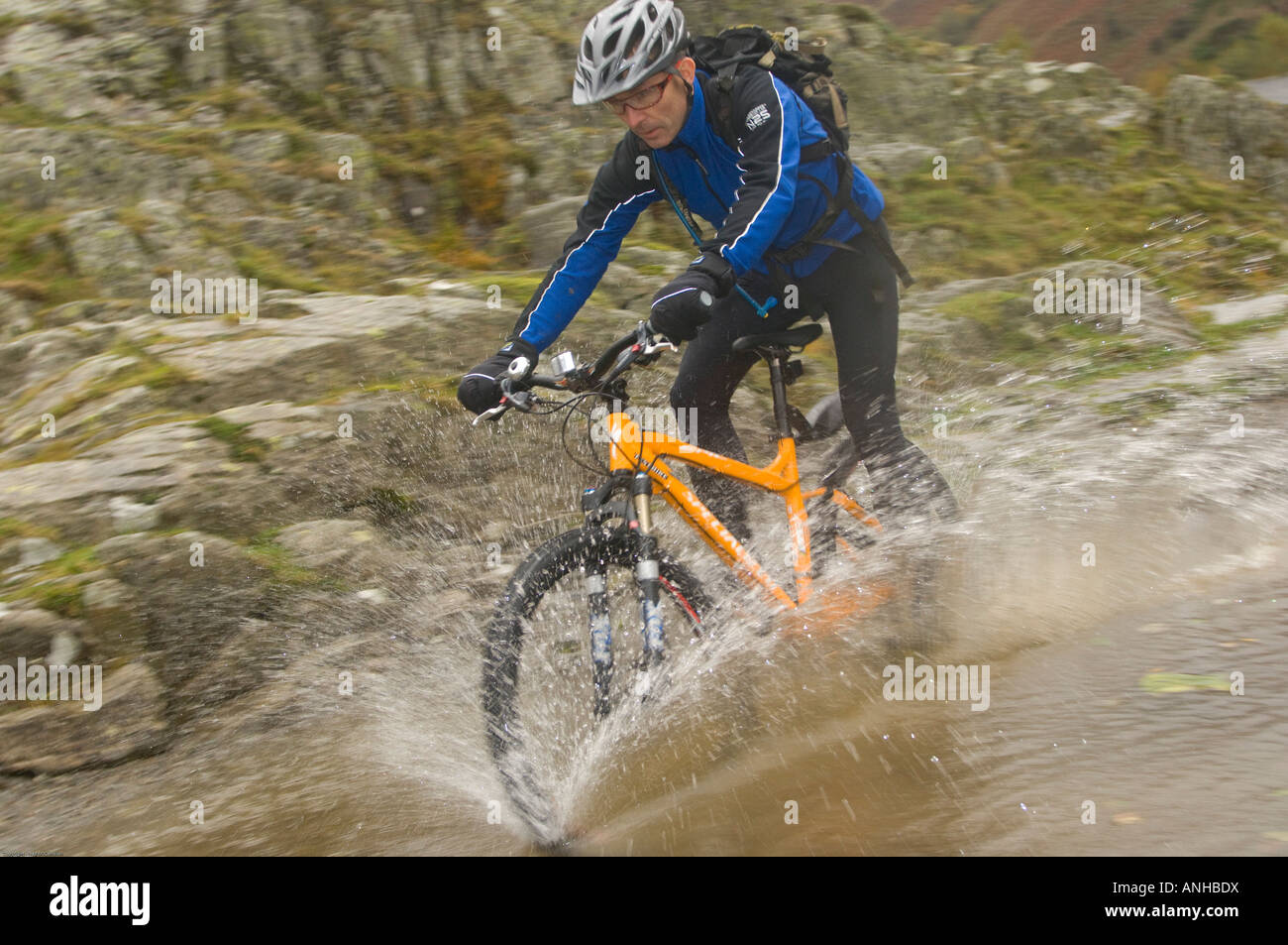 A mountain biker splash through a river on a rainy day in the Lake ...