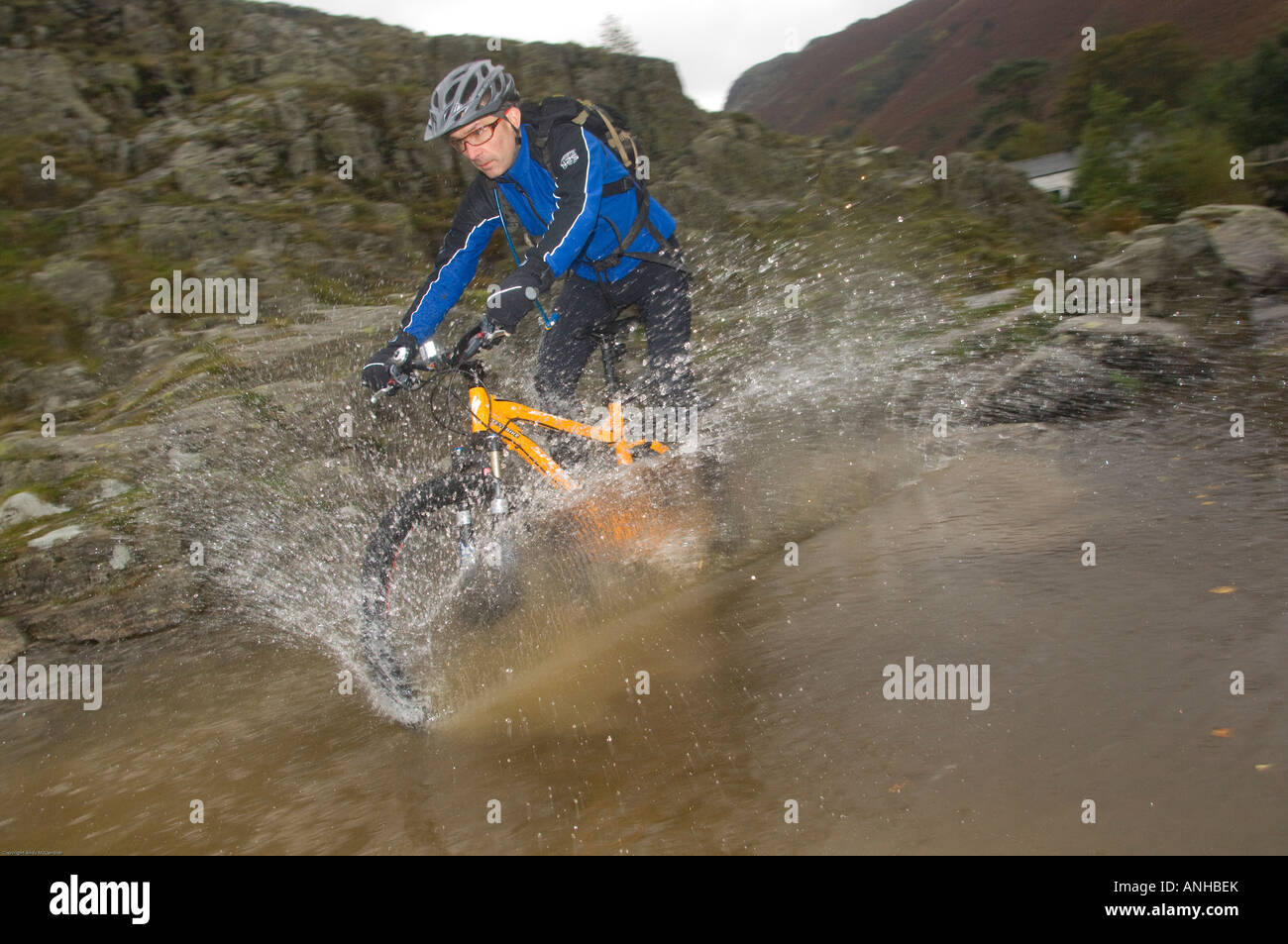 A mountain biker splash through a river on a rainy day in the Lake ...