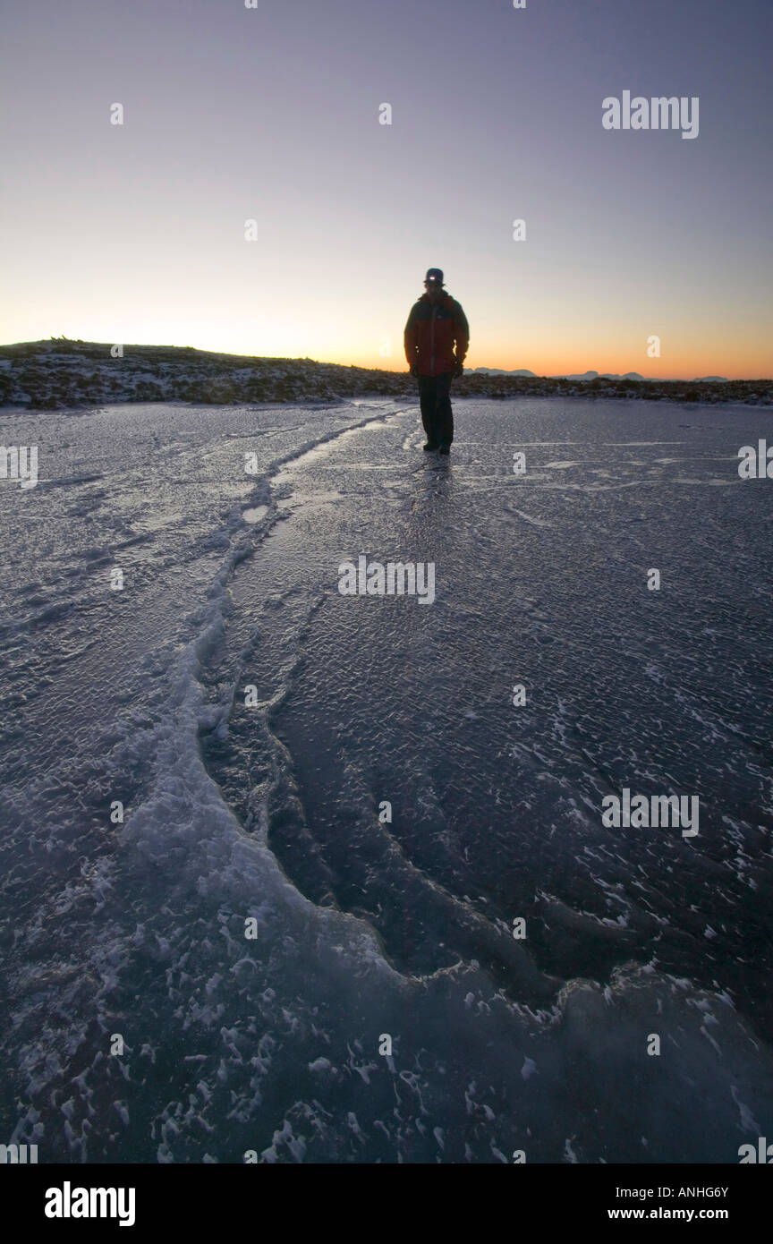 A walker on a frozen tarn on the summit of Red Screes in the Lake ...