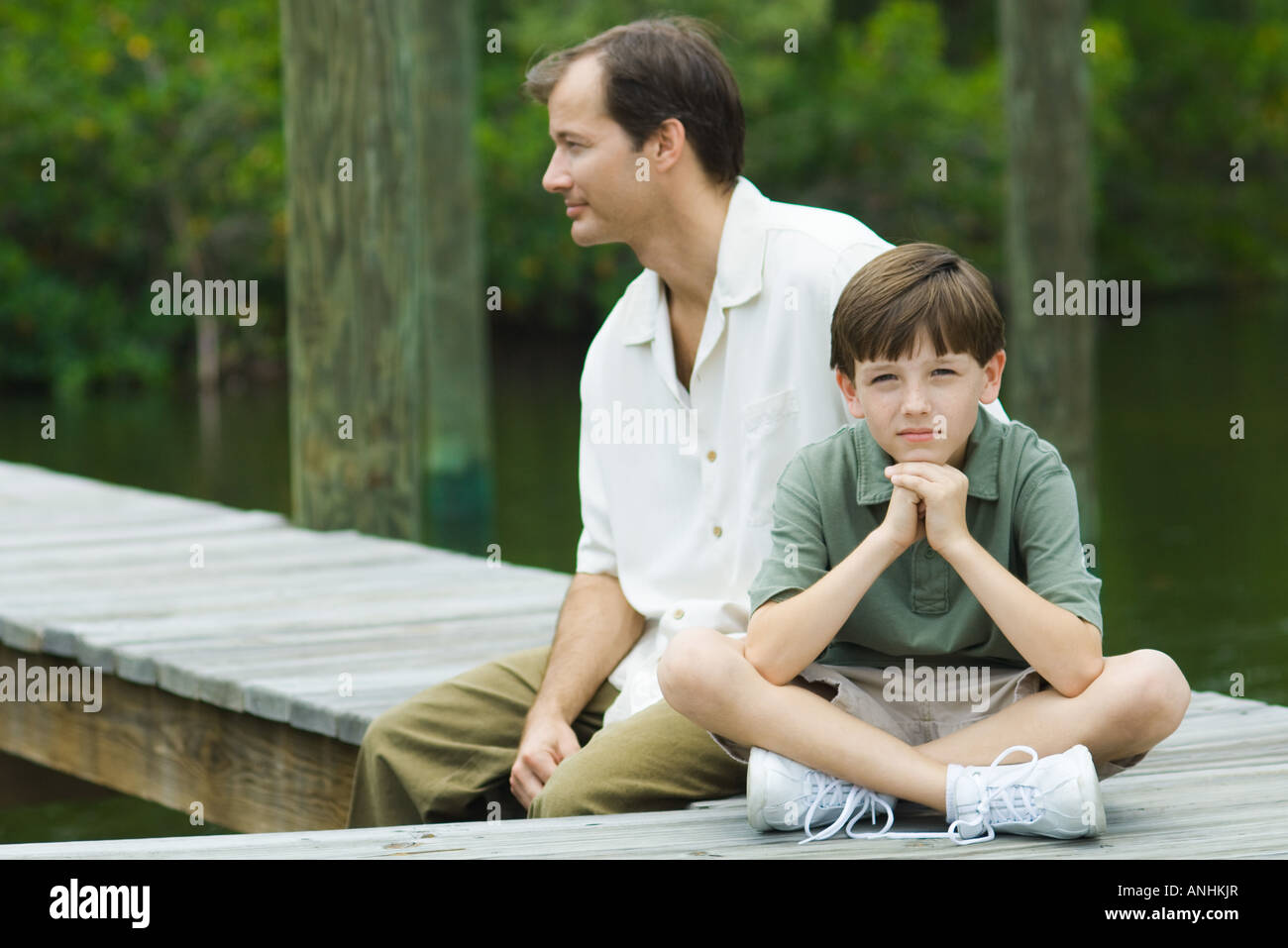 Boy sitting on dock with father, smiling at camera Stock Photo - Alamy