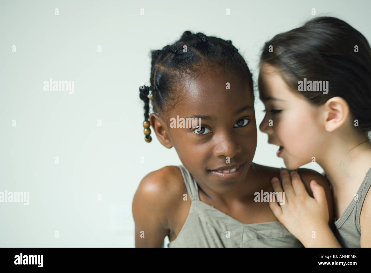 Girl looking at camera as friend whispers in her ear Stock Photo - Alamy