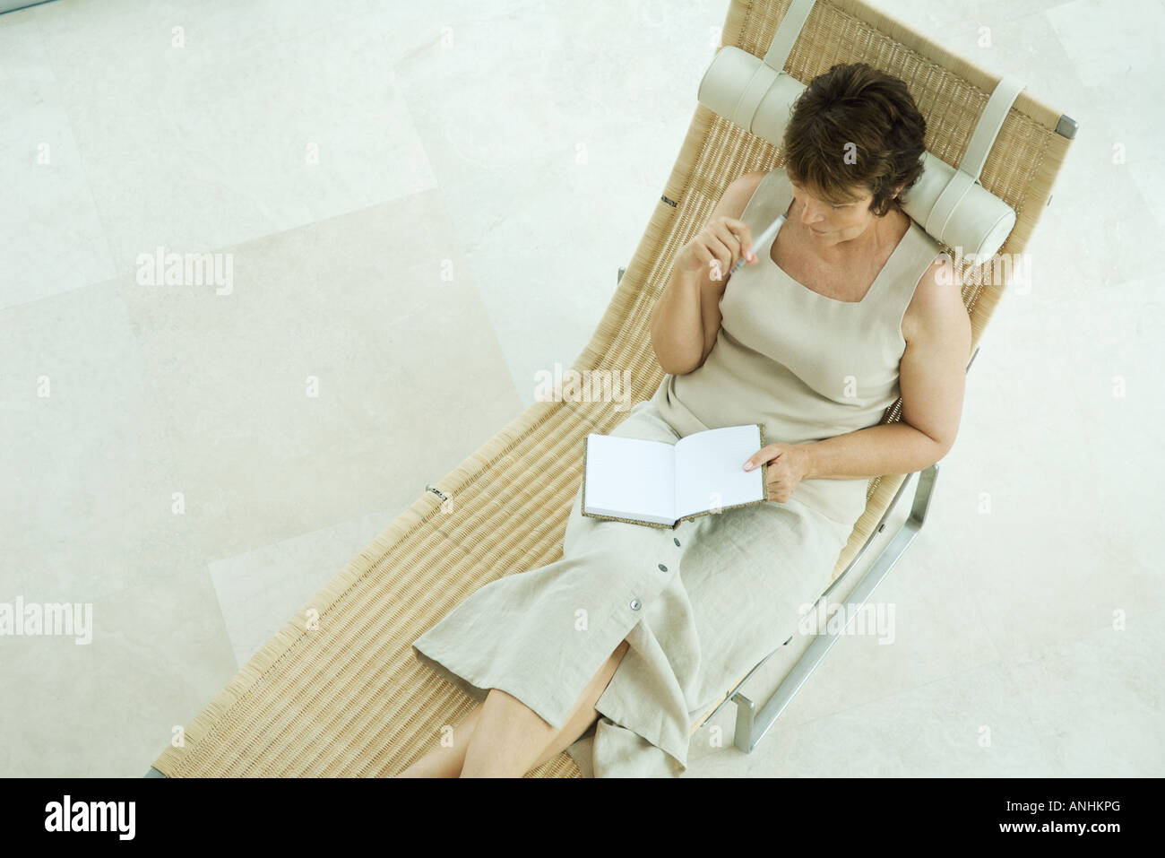 Woman sitting on lounge chair writing in diary, high angle view Stock ...
