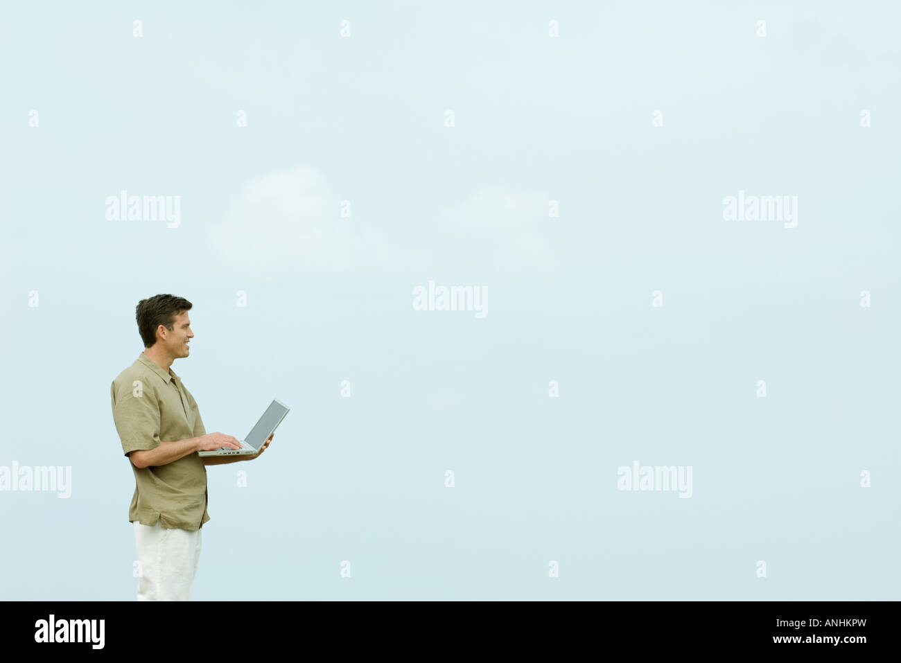 Man standing outdoors holding laptop computer, looking away Stock Photo ...