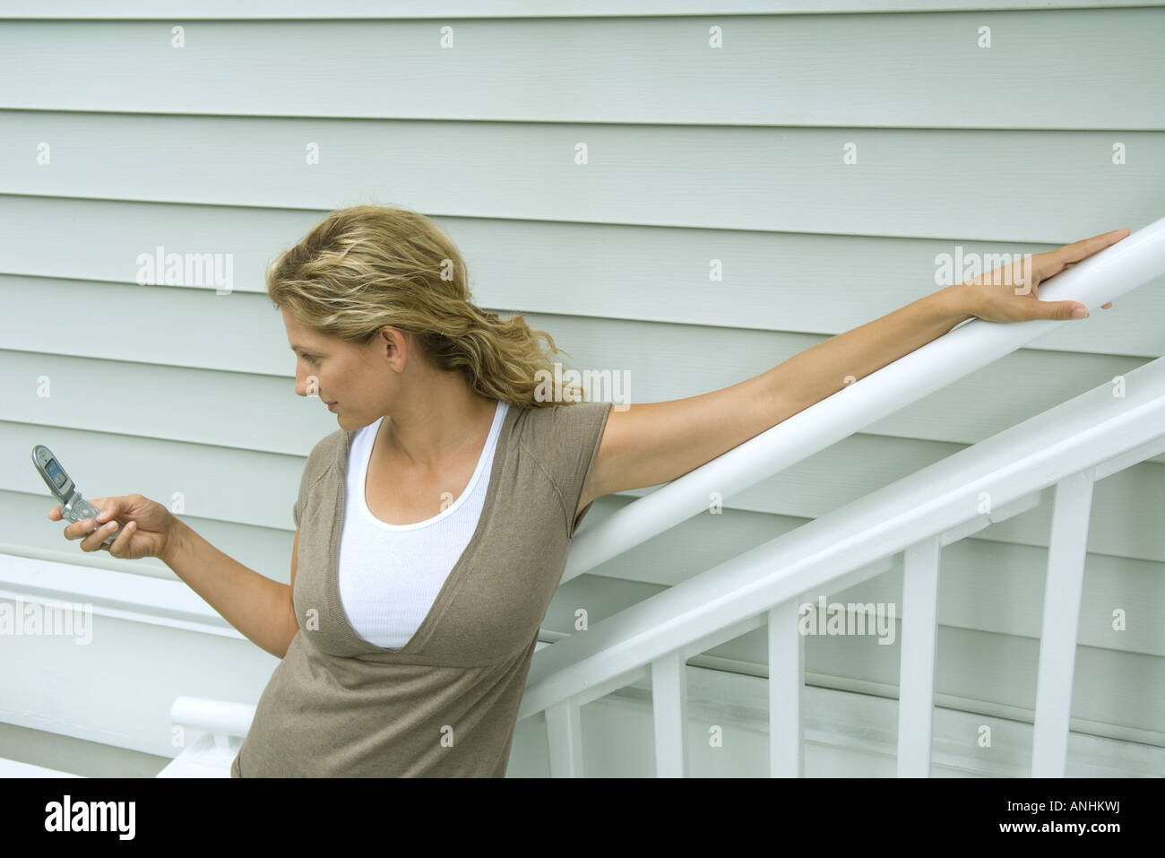 Woman leaning against railing, looking down at cell phone Stock Photo ...