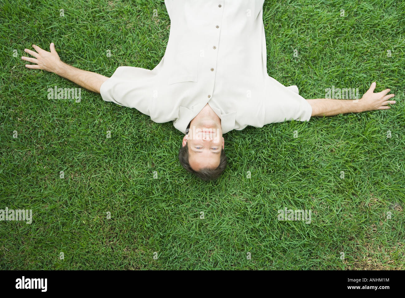 Man lying on back on grass, smiling at camera, viewed from directly ...