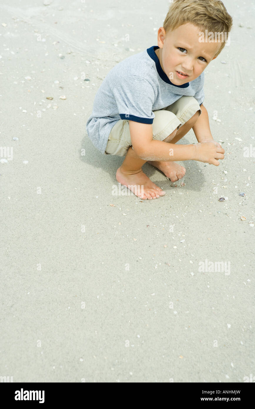 Boy crouching in sand, looking up at camera Stock Photo - Alamy