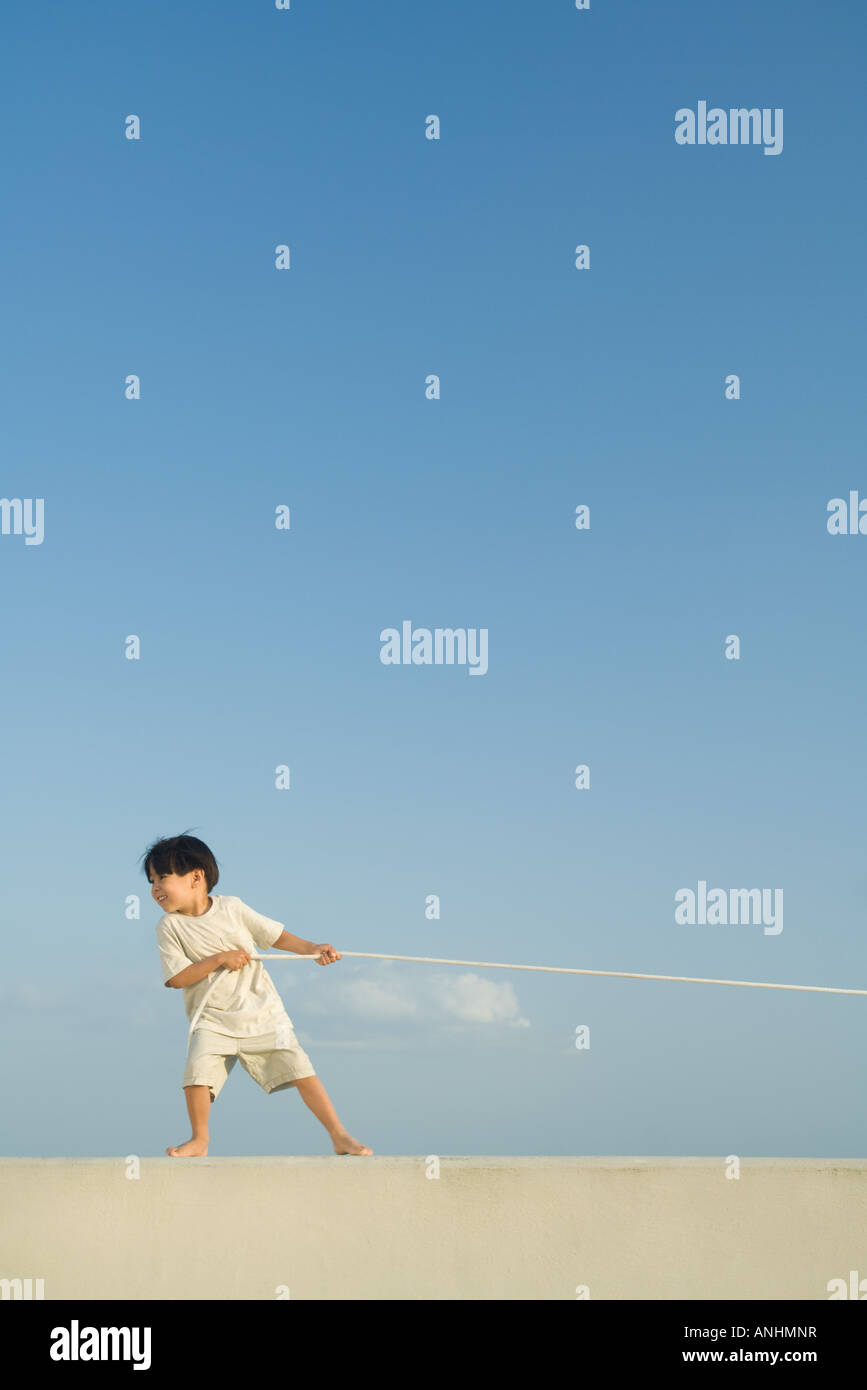Little boy pulling on rope, blue sky in background, full length Stock ...