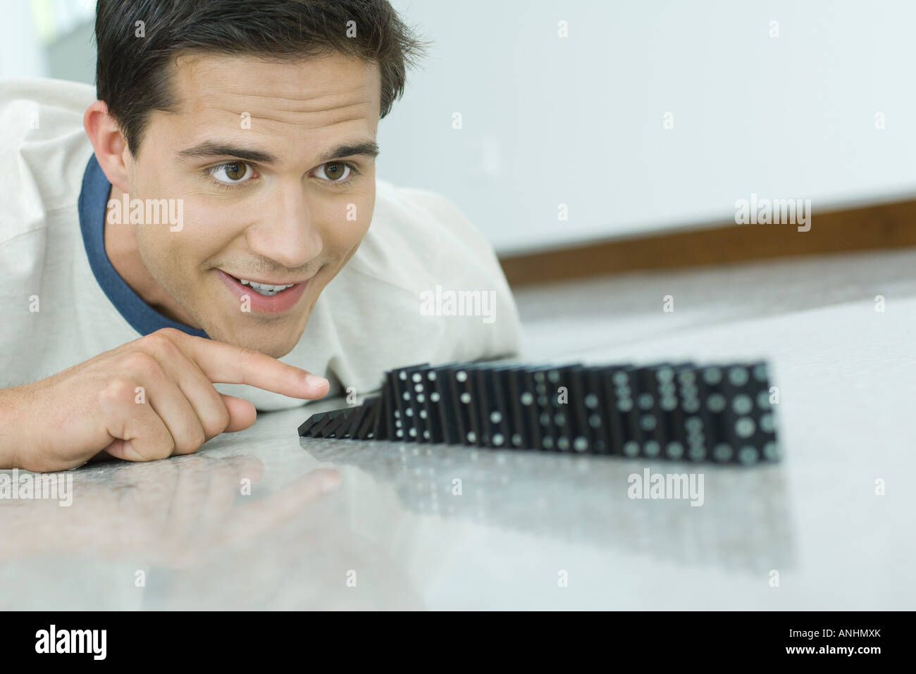 Young man knocking over line of dominos Stock Photo - Alamy