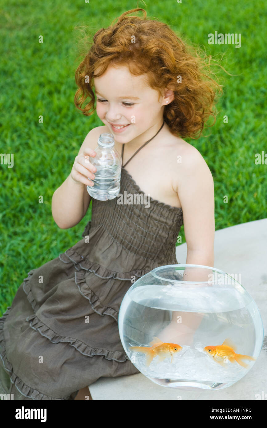 Girl sitting next to goldfish bowl, drinking water Stock Photo - Alamy