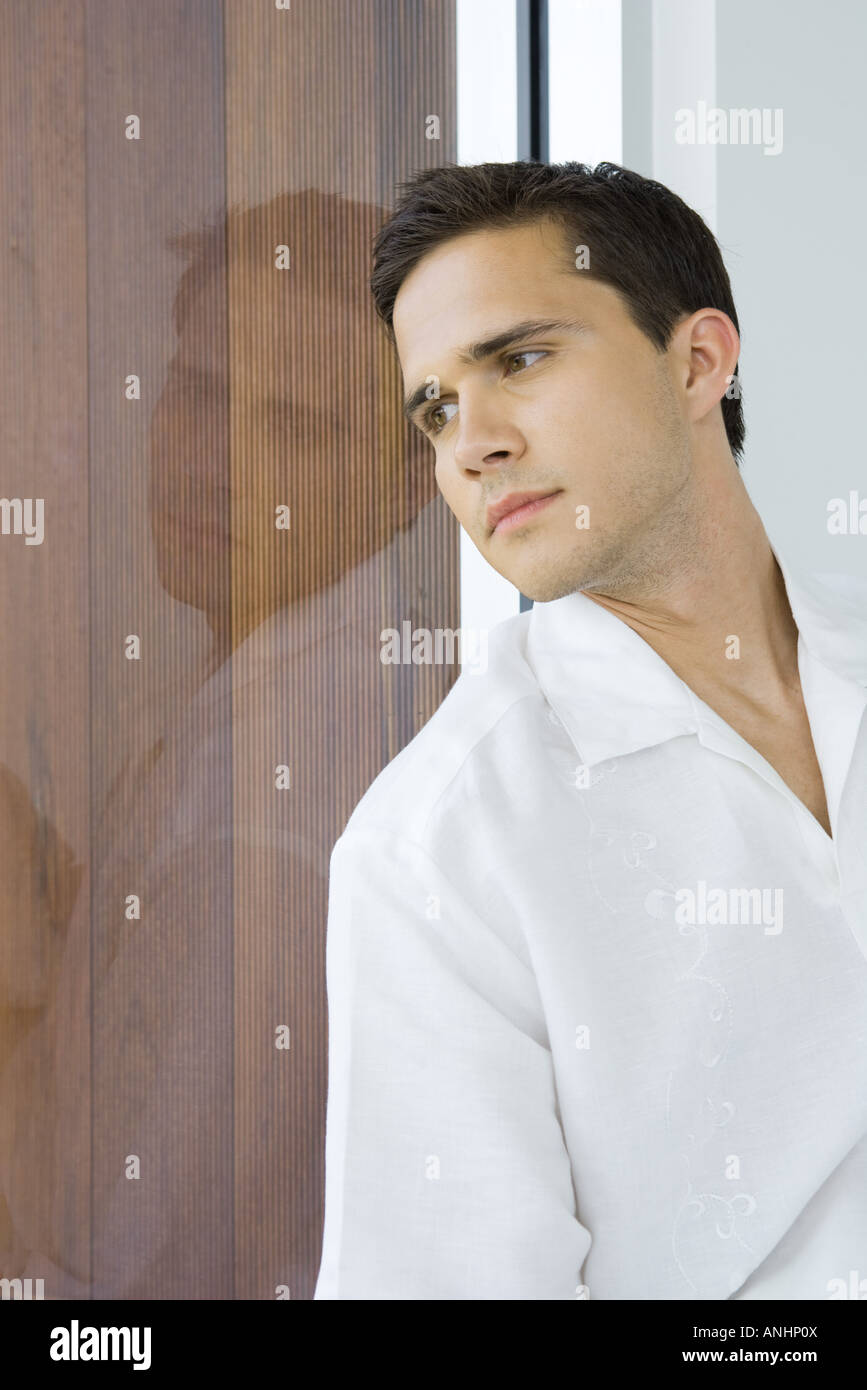 Young man leaning against window, looking out, close-up Stock Photo - Alamy