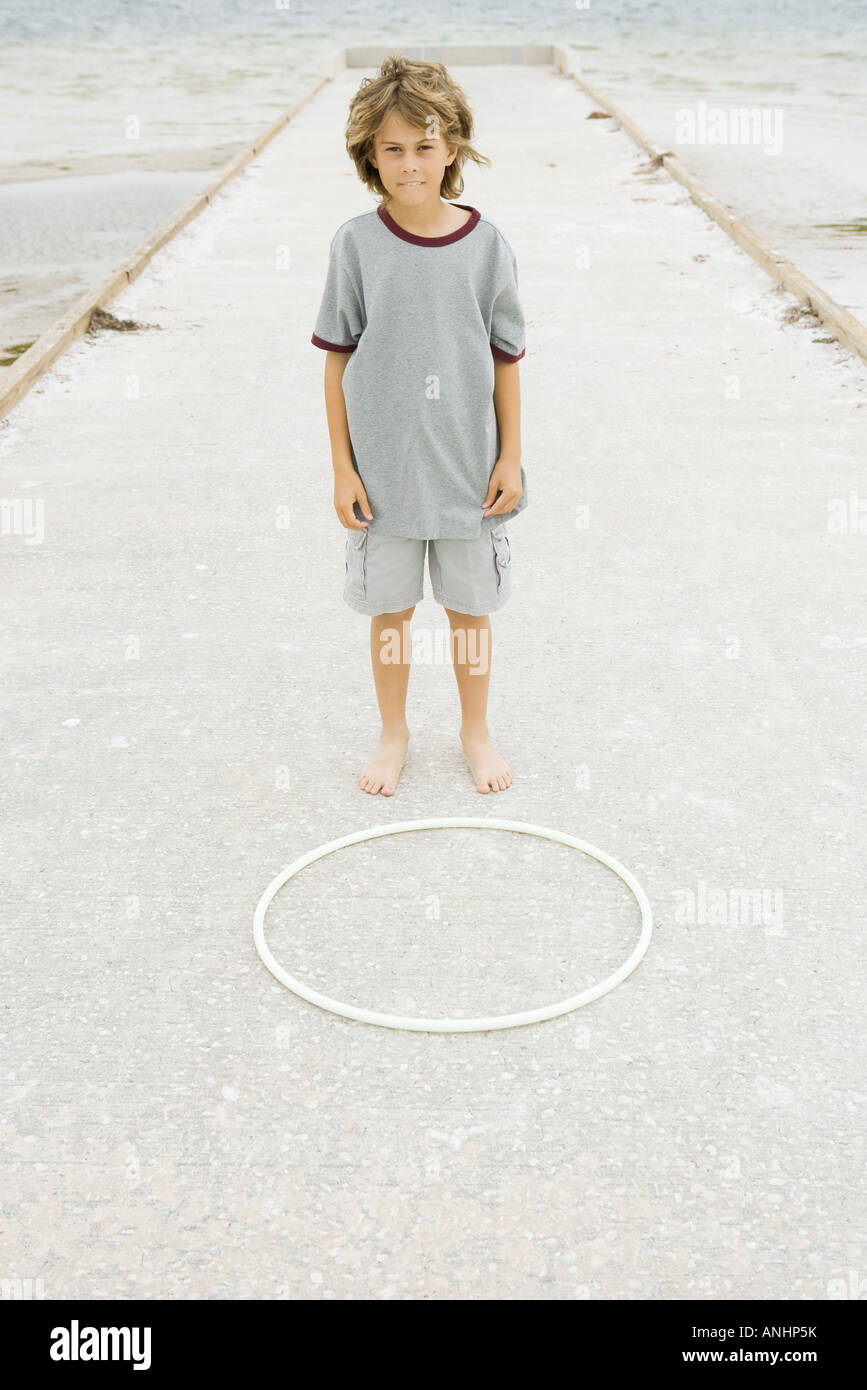 Boy standing on pier in front of plastic hoop, looking at camera and ...
