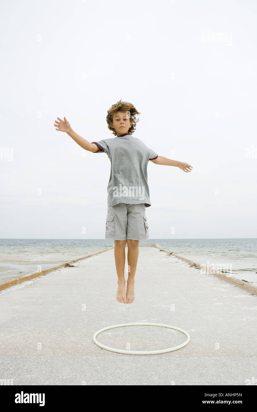 Boy jumping over plastic hoop with arms out, looking at camera Stock ...