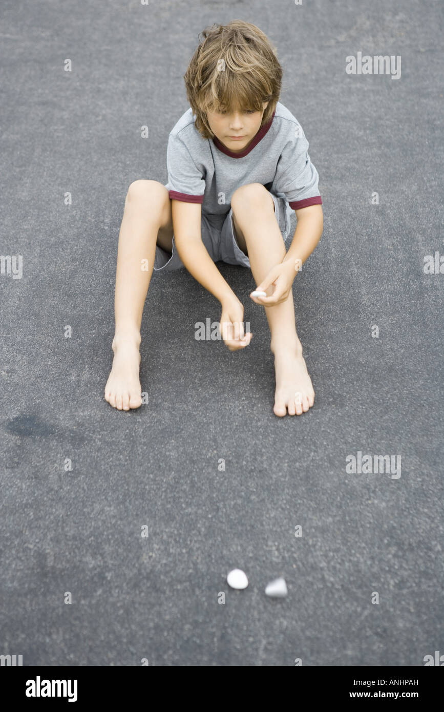 Boy sitting on the ground throwing pebbles, high angle view Stock Photo ...