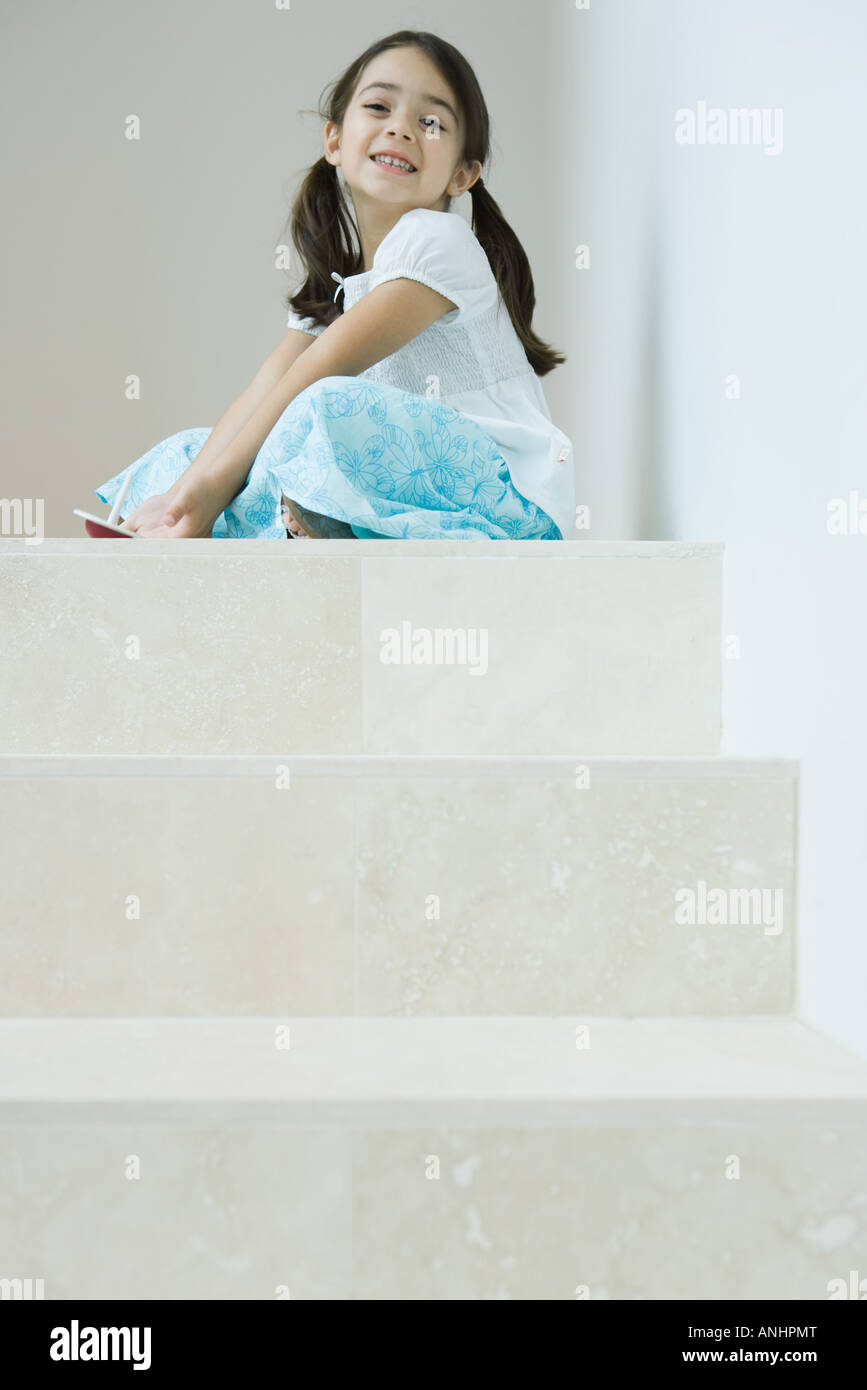 Girl sitting on steps playing with top, smiling at camera, low angle ...